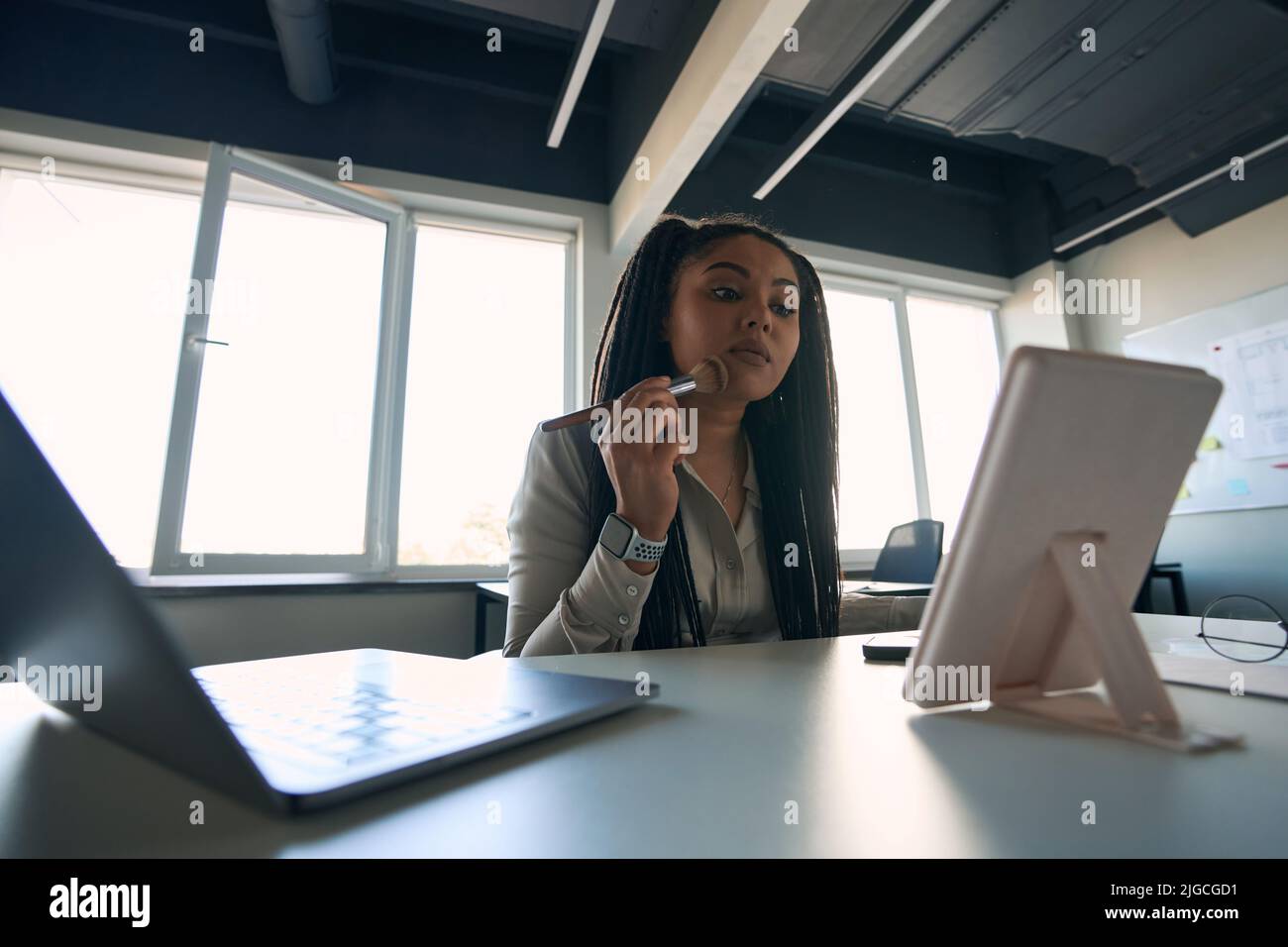 Focused corporate employee looking in tabletop mirror during makeup ...