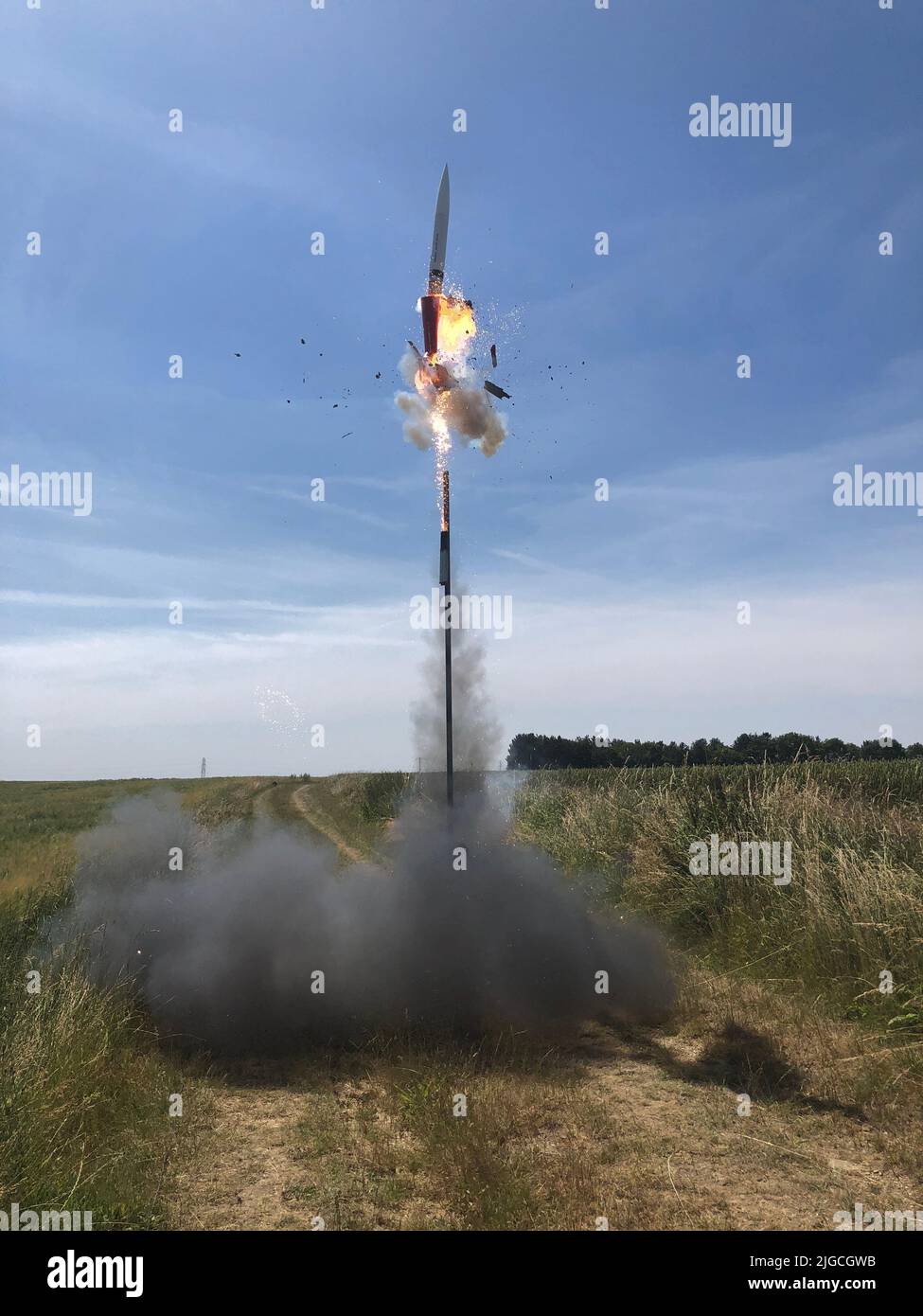 A vertical shot of a rocket flying from a green field to a cloudy sky ...