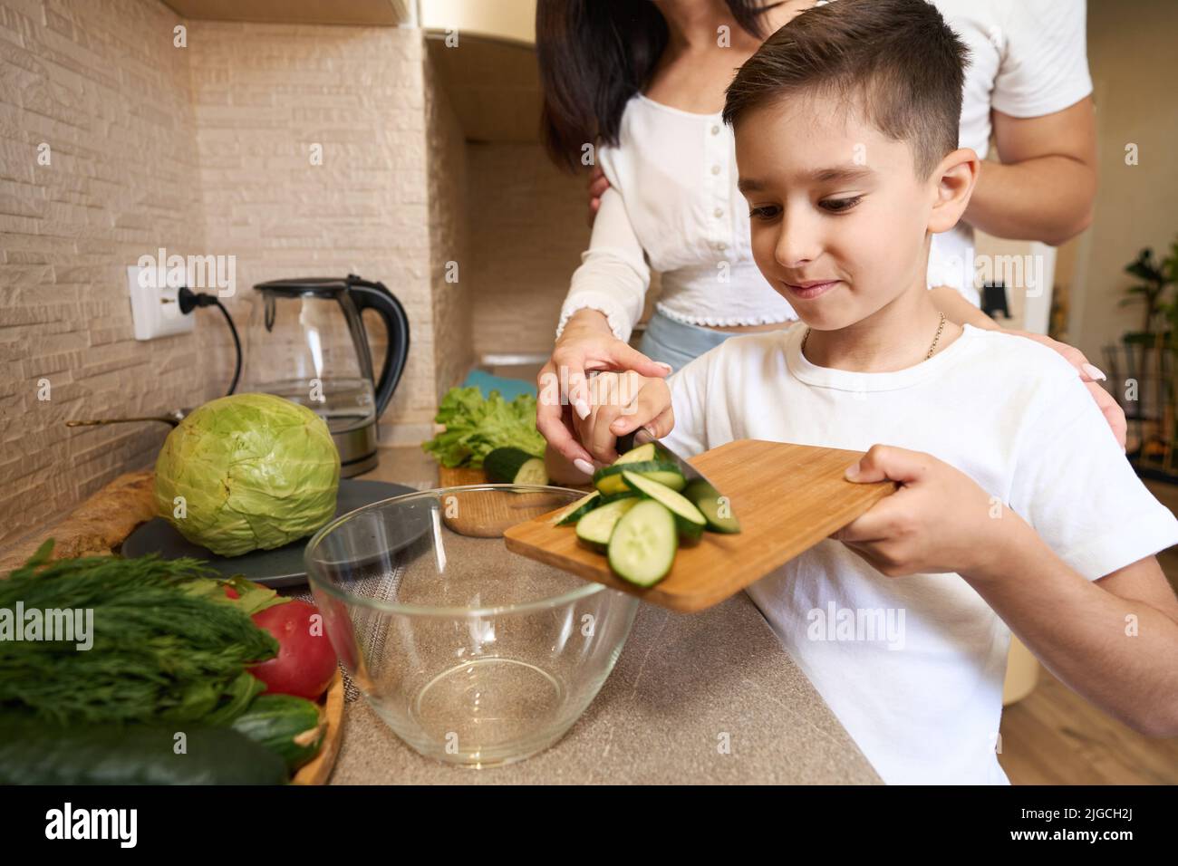 Boy throwing cucumber slices from cutting board into bowl Stock Photo ...