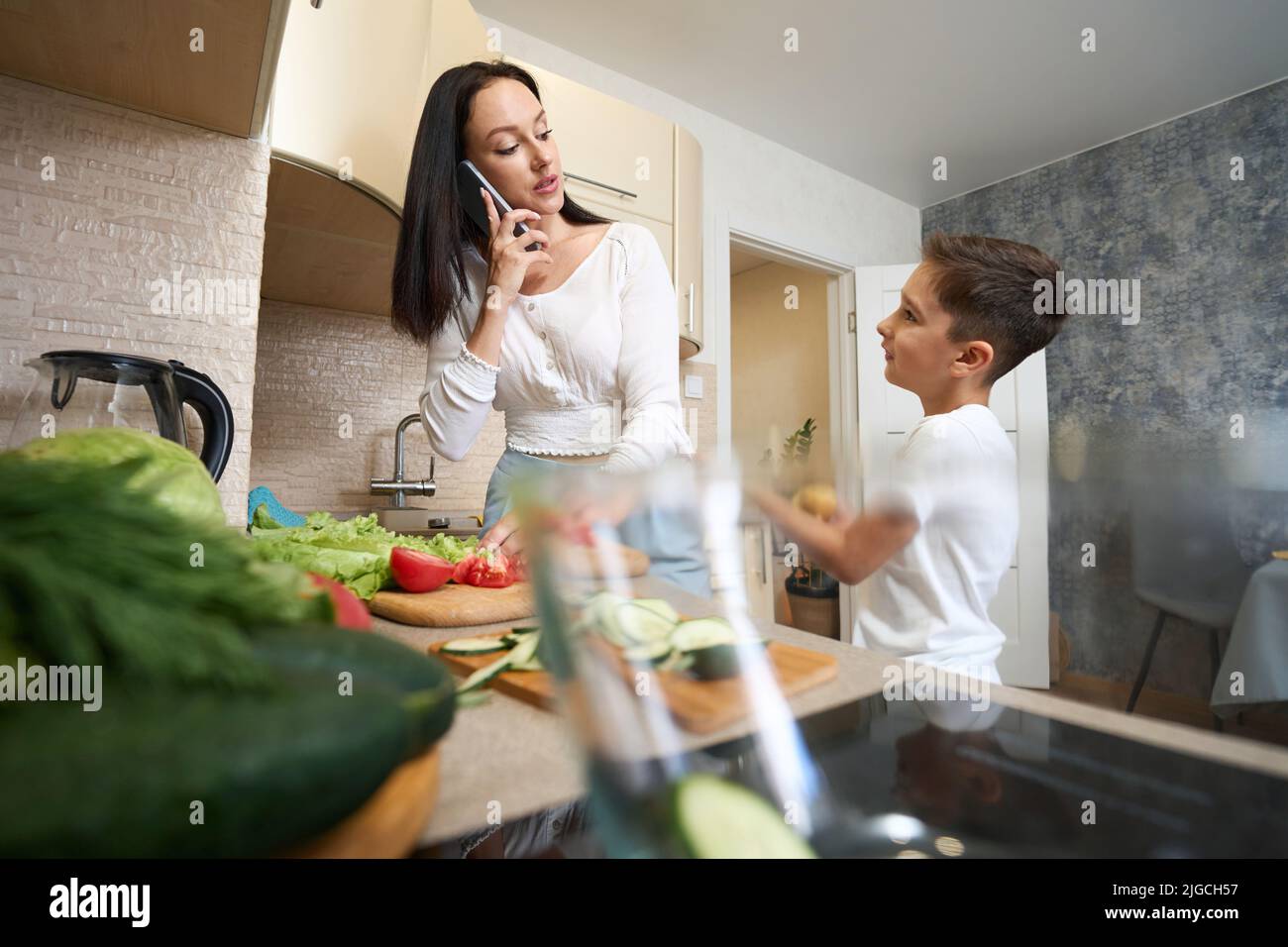 Mother answering child question while cooking and talking on smartphone ...