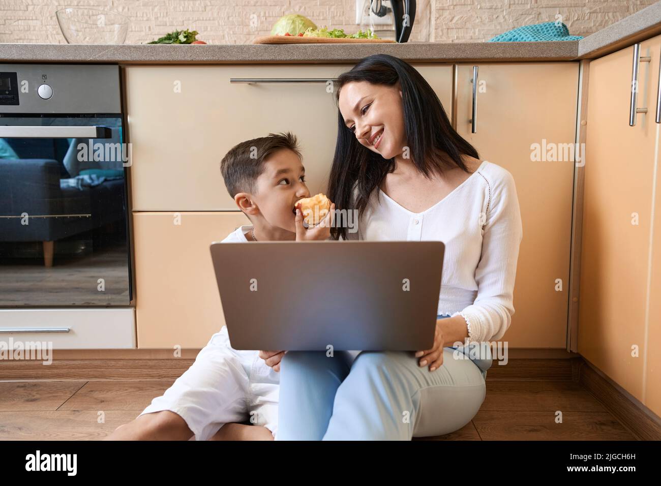 Kid biting apple while working with laptop near mother Stock Photo - Alamy