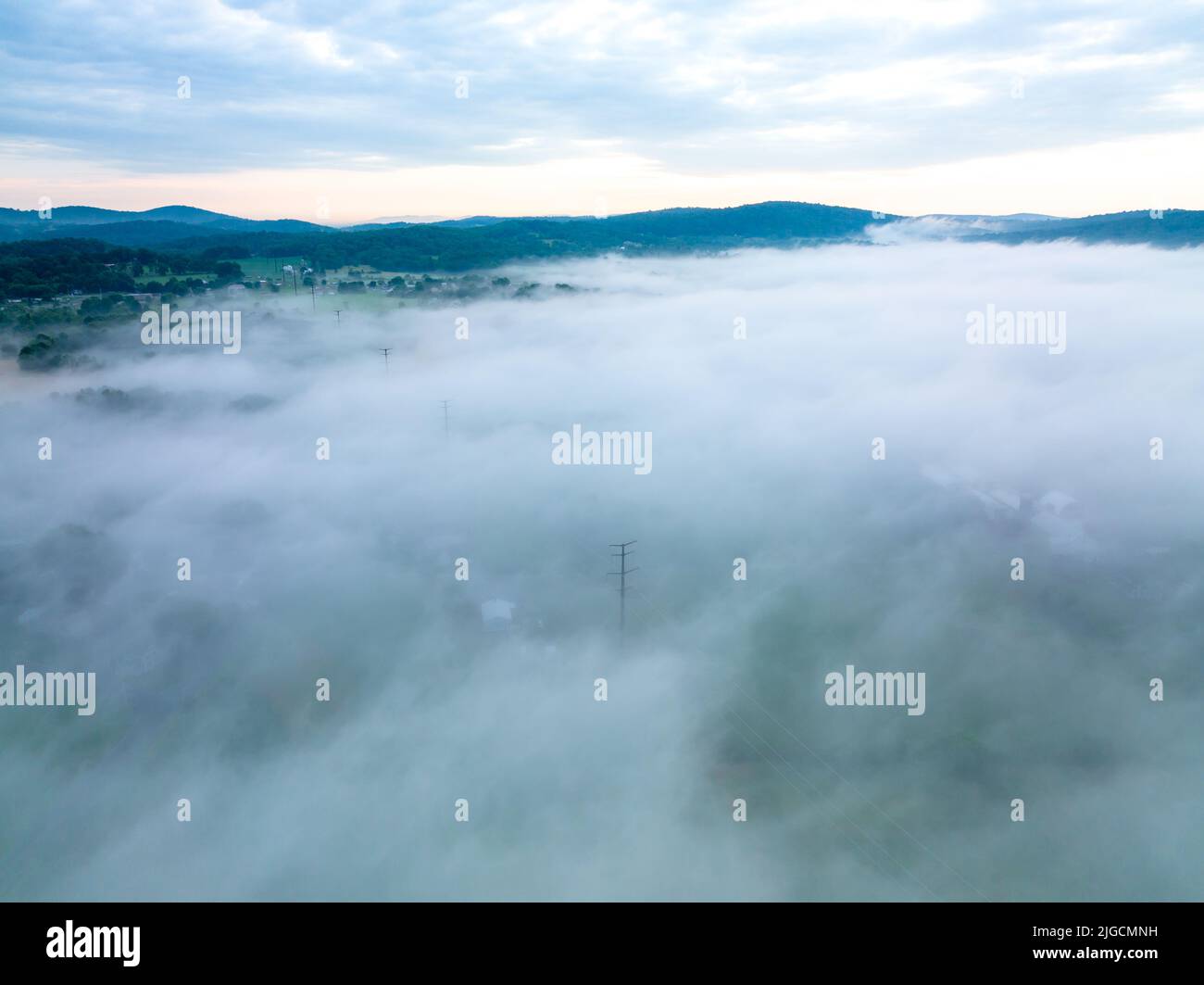 An aerial view from above the fog as it covers the landscape, fields ...