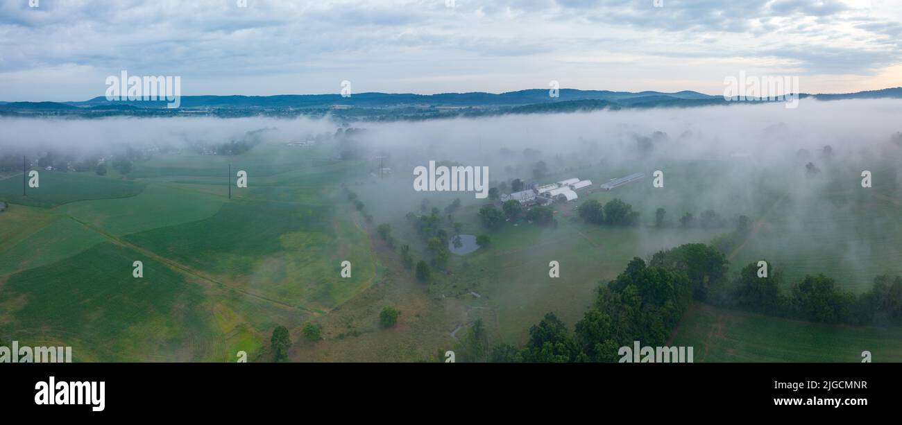 An aerial view from above the fog as it covers the landscape, fields ...