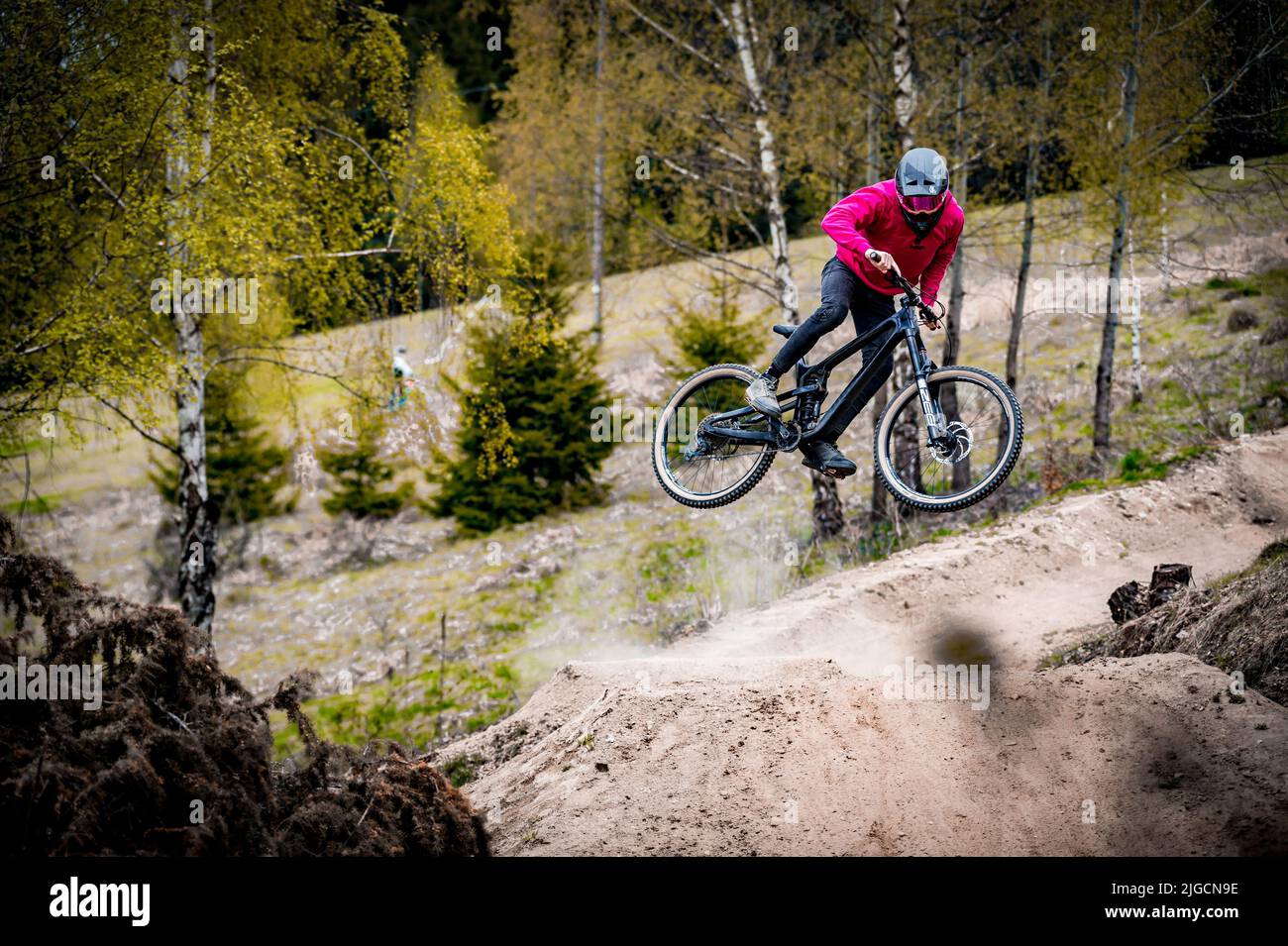 A male rider in a helmet on a bike jumping over a track at a bike park ...