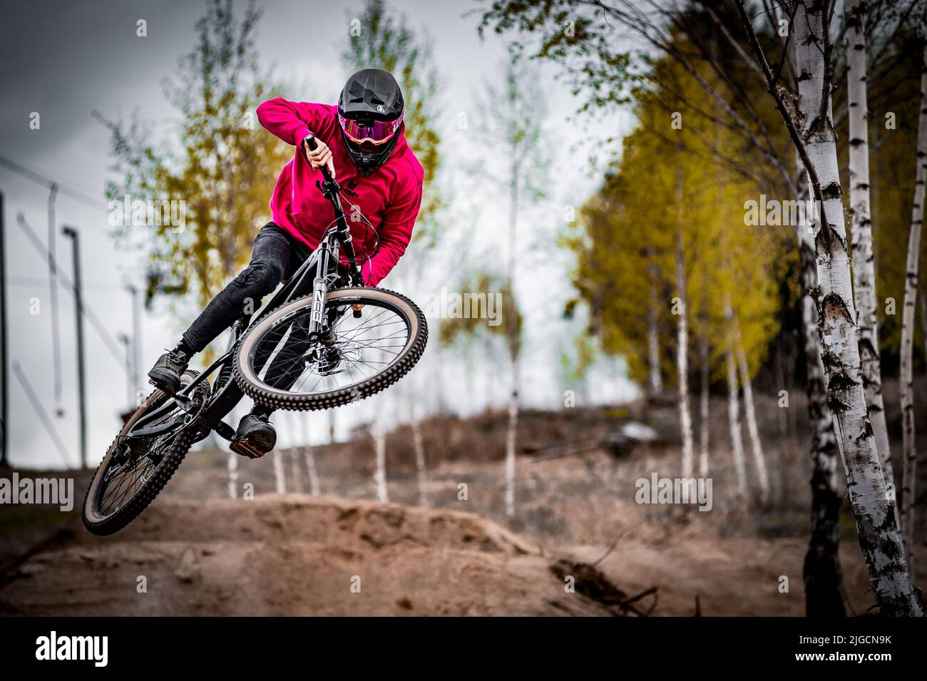 A male rider in a helmet on a bike jumping over a track at a bike park ...