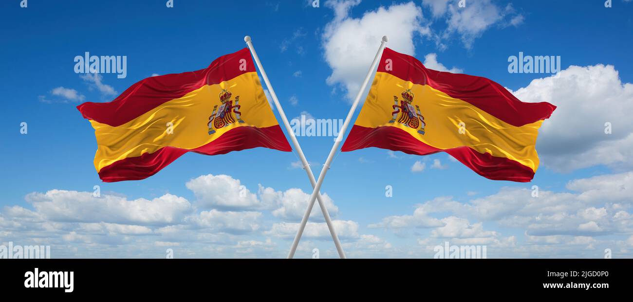 two crossed flags of Spain waving in wind at cloudy sky. Concept of ...