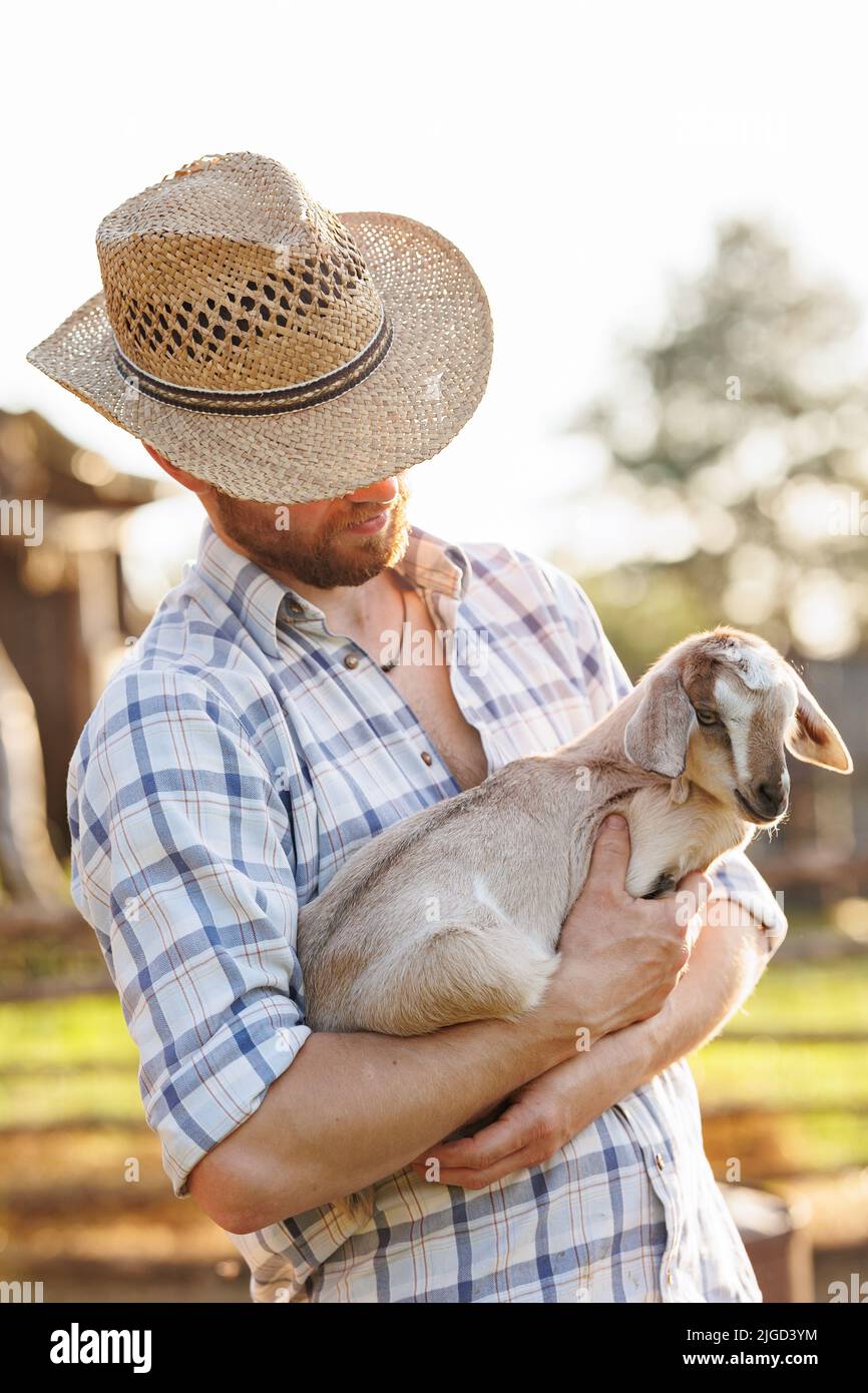 Portrait of young Caucasian bearded male farmer in straw hat holding a ...