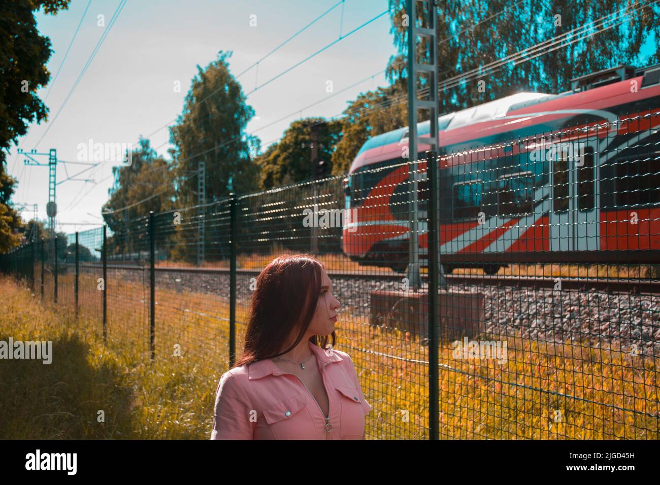A Caucasian beautiful walking along side the train behind a metal fence ...