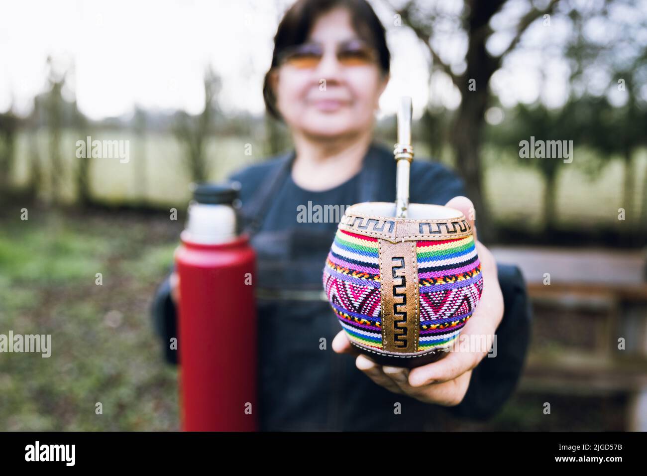 Latin woman serving mate with a red thermo, in a colorful ethnic mate ...