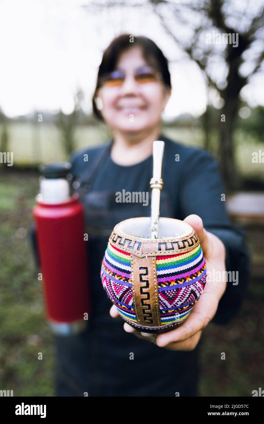 Latin woman serving mate with a red thermo, in a colorful ethnic mate ...