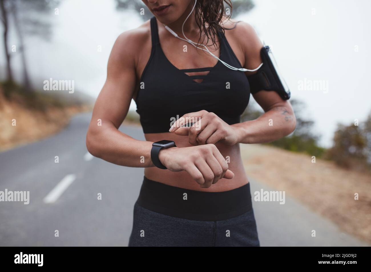 Sporty young woman adjusting her smartwatch while exercising outdoors ...