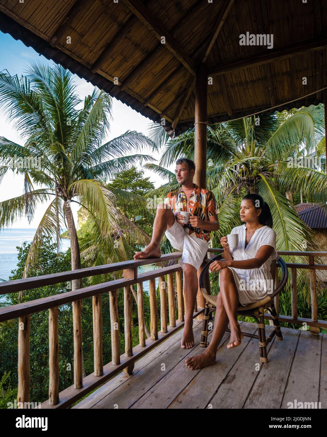 a couple of men and women on the balcony of a beach hut with coffee in ...
