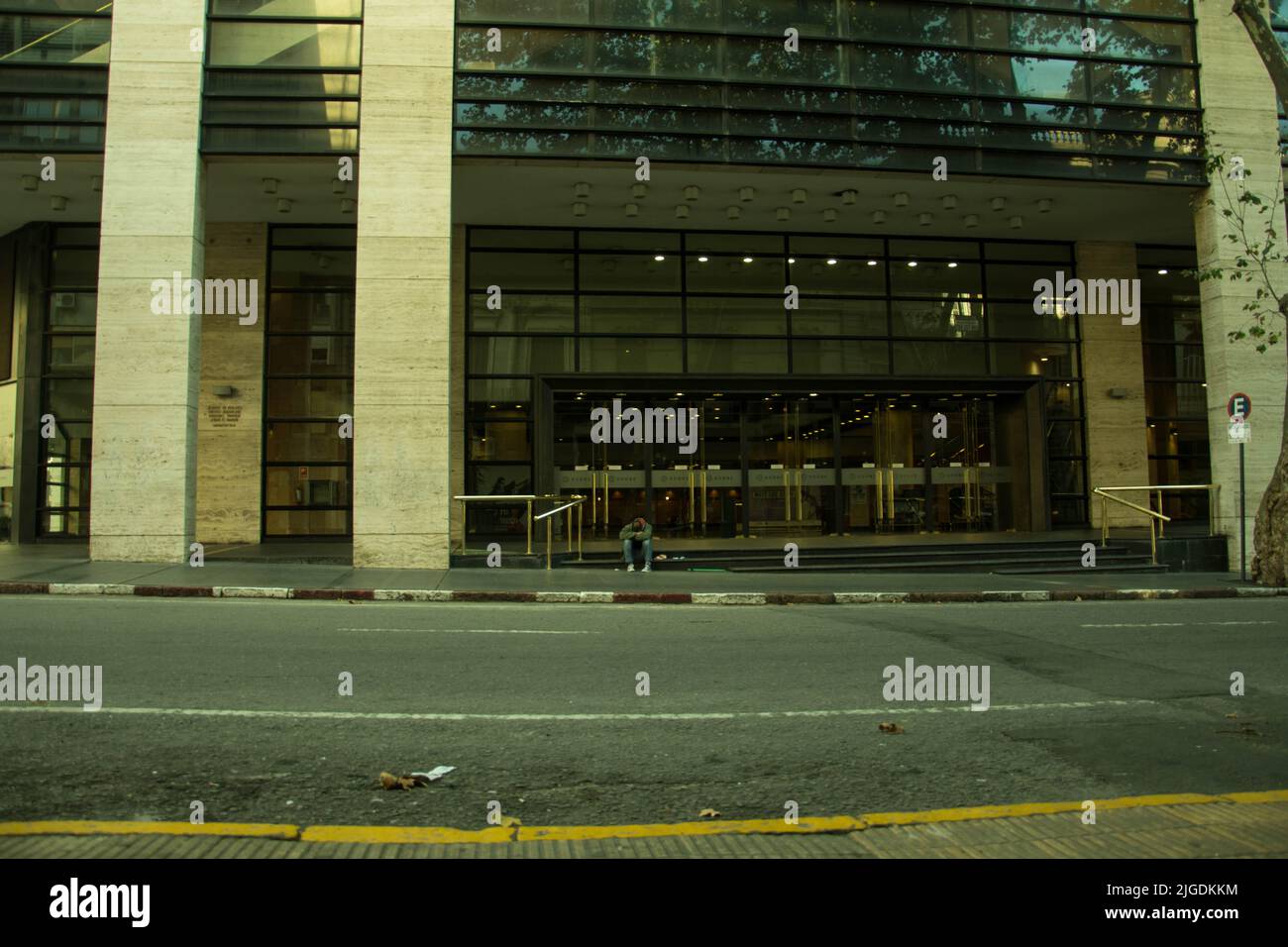 A man sitting on the side of a street in front of a building Stock ...