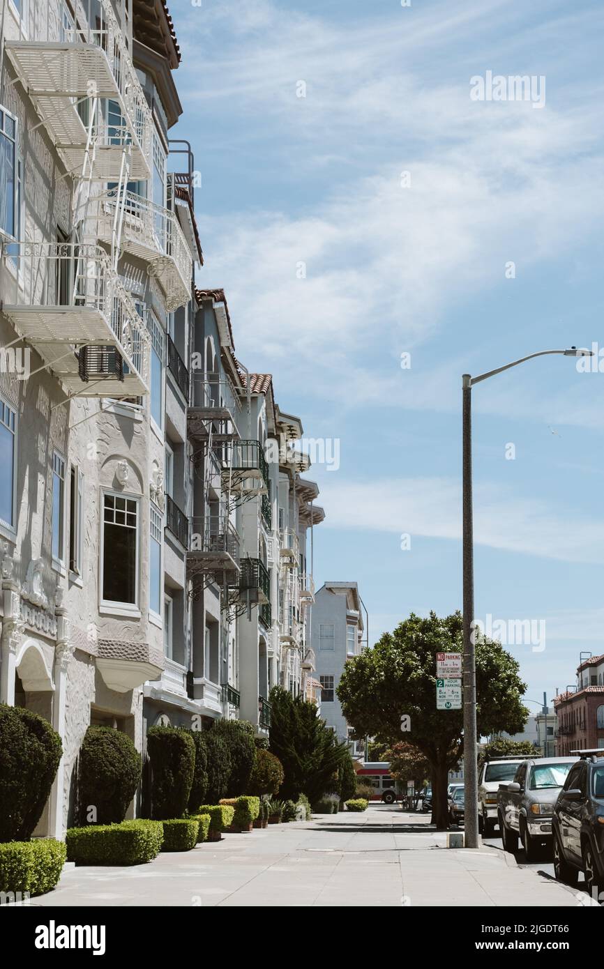 A vertical shot of empty street and facade of white buildings, parked ...