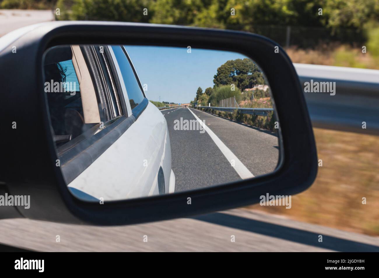 Rearview mirror of a white car driving on a highway, which is reflected ...