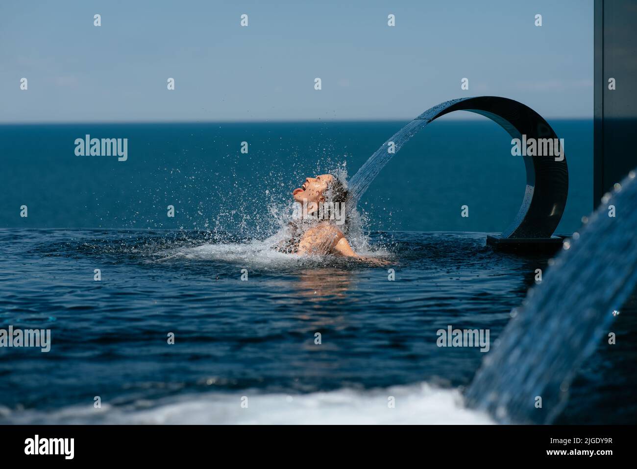 Young woman relaxing under swimming pool waterfall jet Stock Photo - Alamy