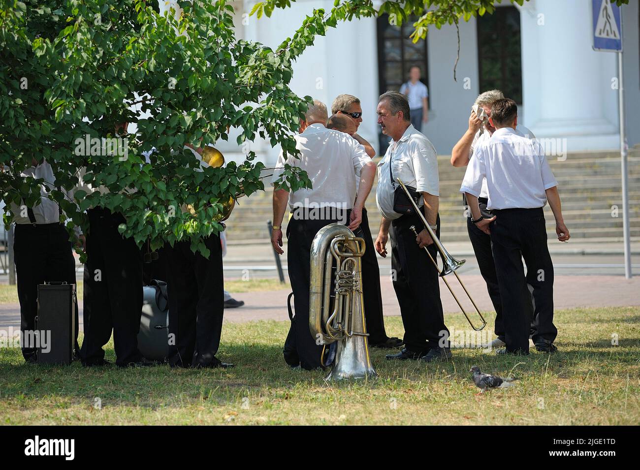 Men musicians from a brass orchestra taking rest standing in the shadow ...