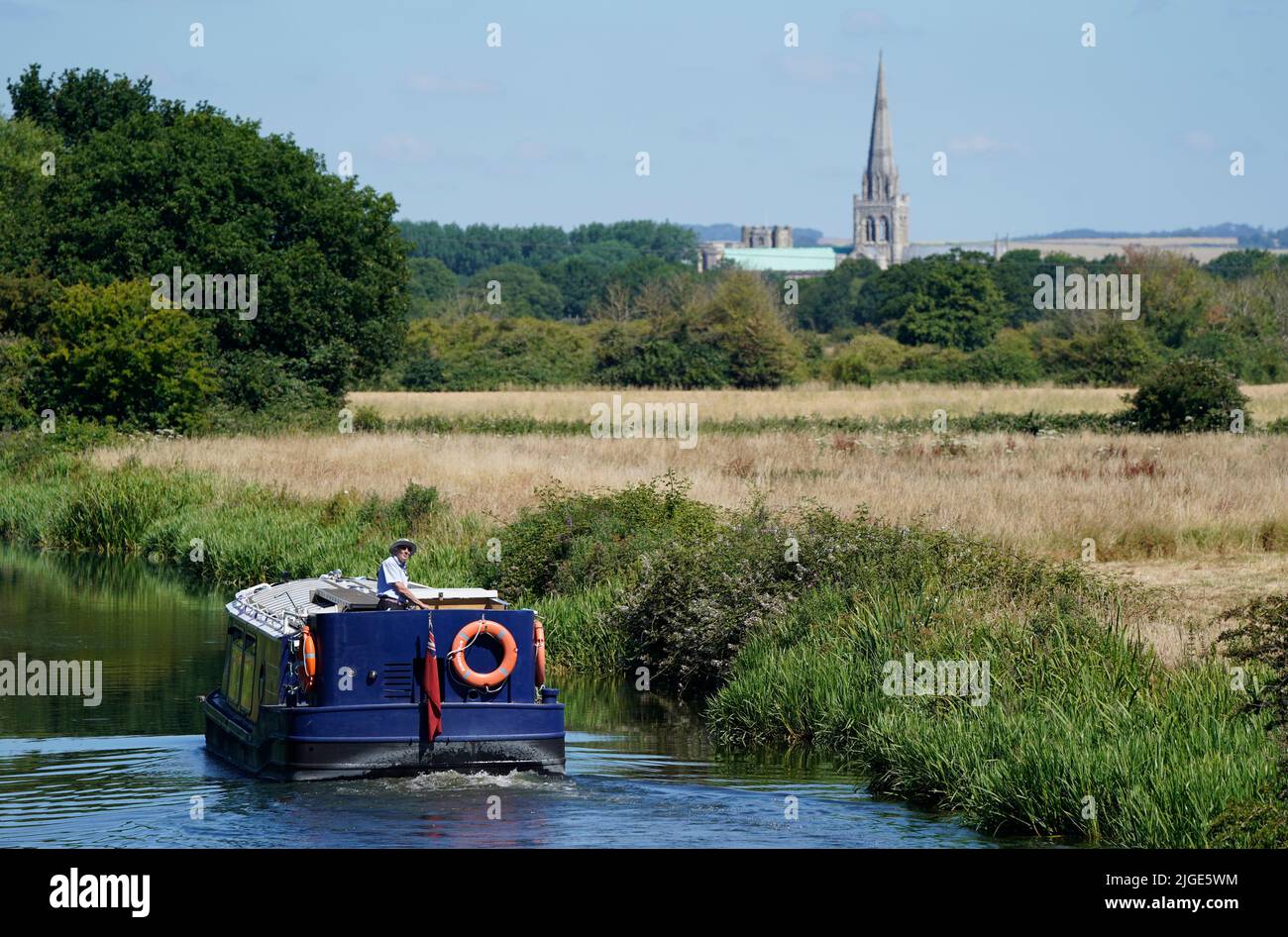 A narrow boat is driven along the Chichester Canal near to Hunston in ...