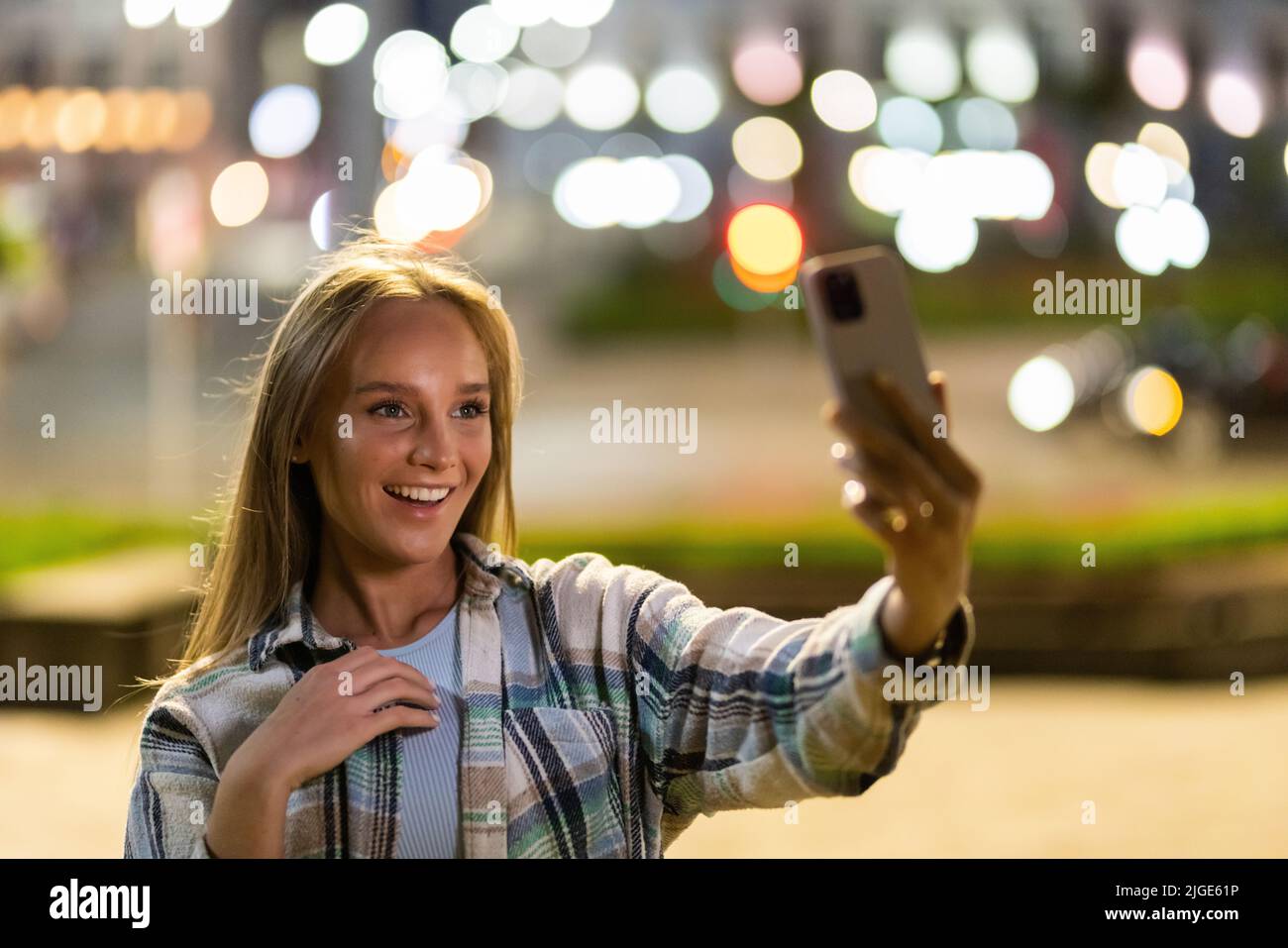 Closeup cheerful girl taking selfie photo by mobile phone on night city ...