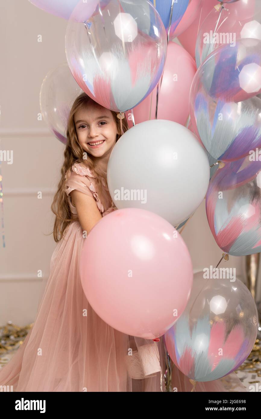 a little beautiful girl in a pink dress on the background of balloons ...