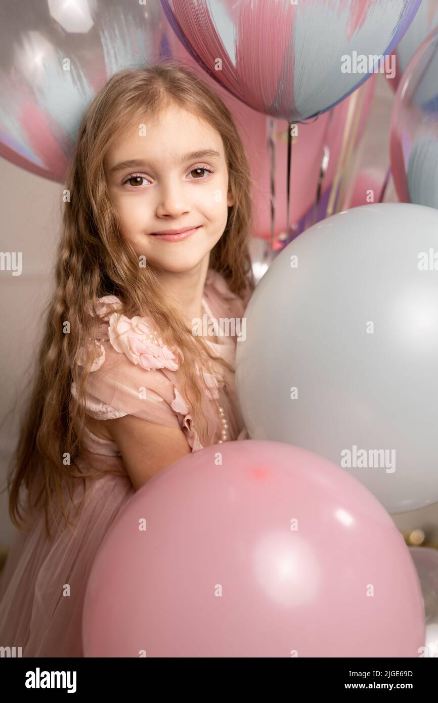 a little beautiful girl in a pink dress on the background of balloons ...