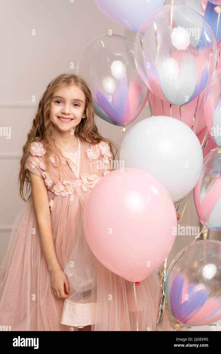 a little beautiful girl in a pink dress on the background of balloons ...