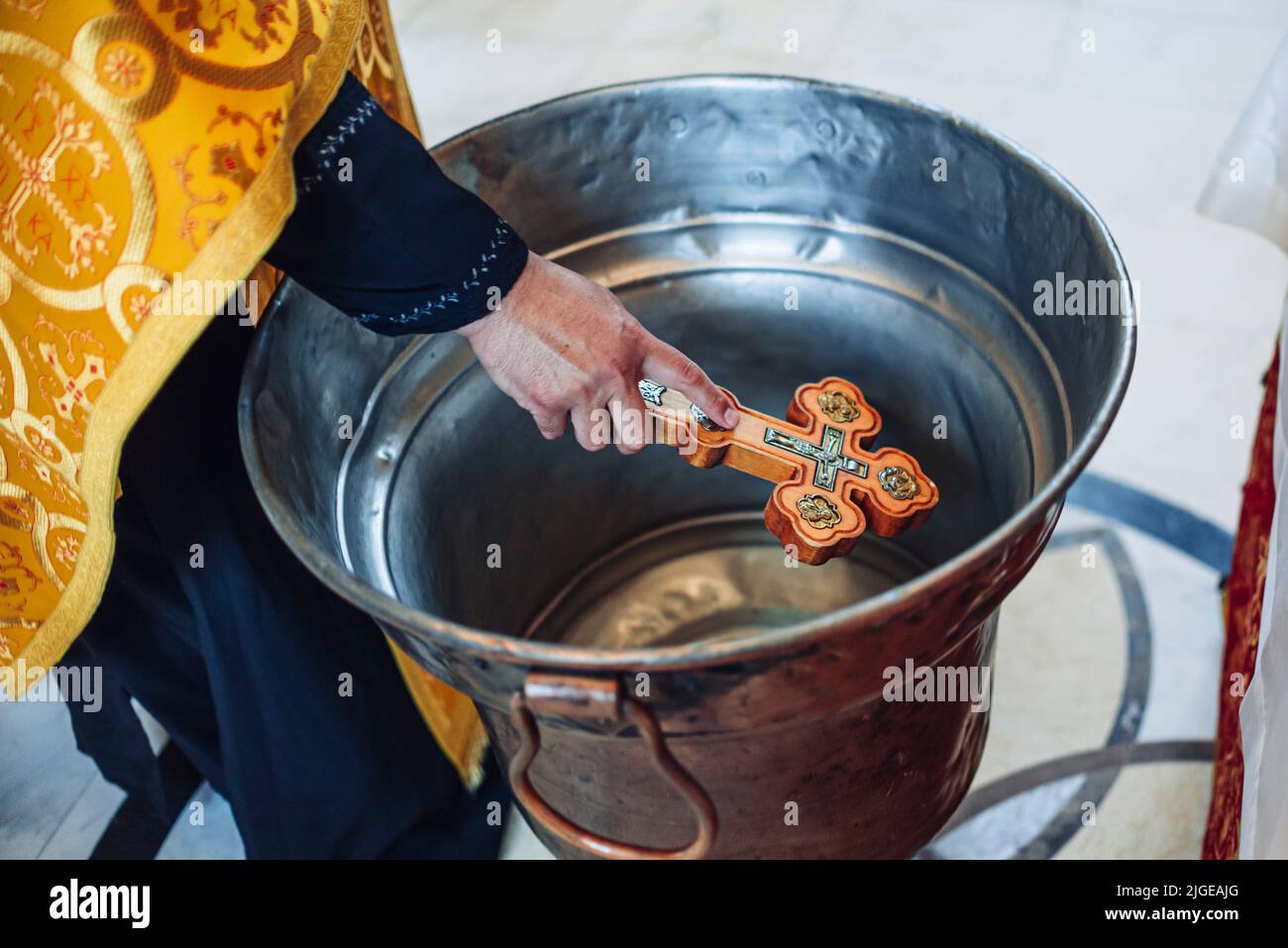 A Bulgarian priest is holding a cross over water for an orthodox baby baptism. High quality ...