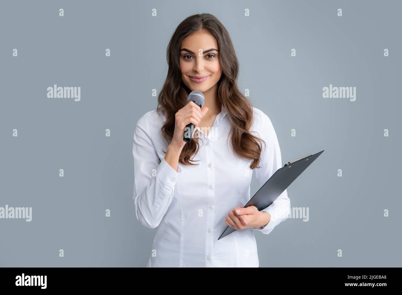 Portrait of young woman journalist in casual shirt holding microphone ...