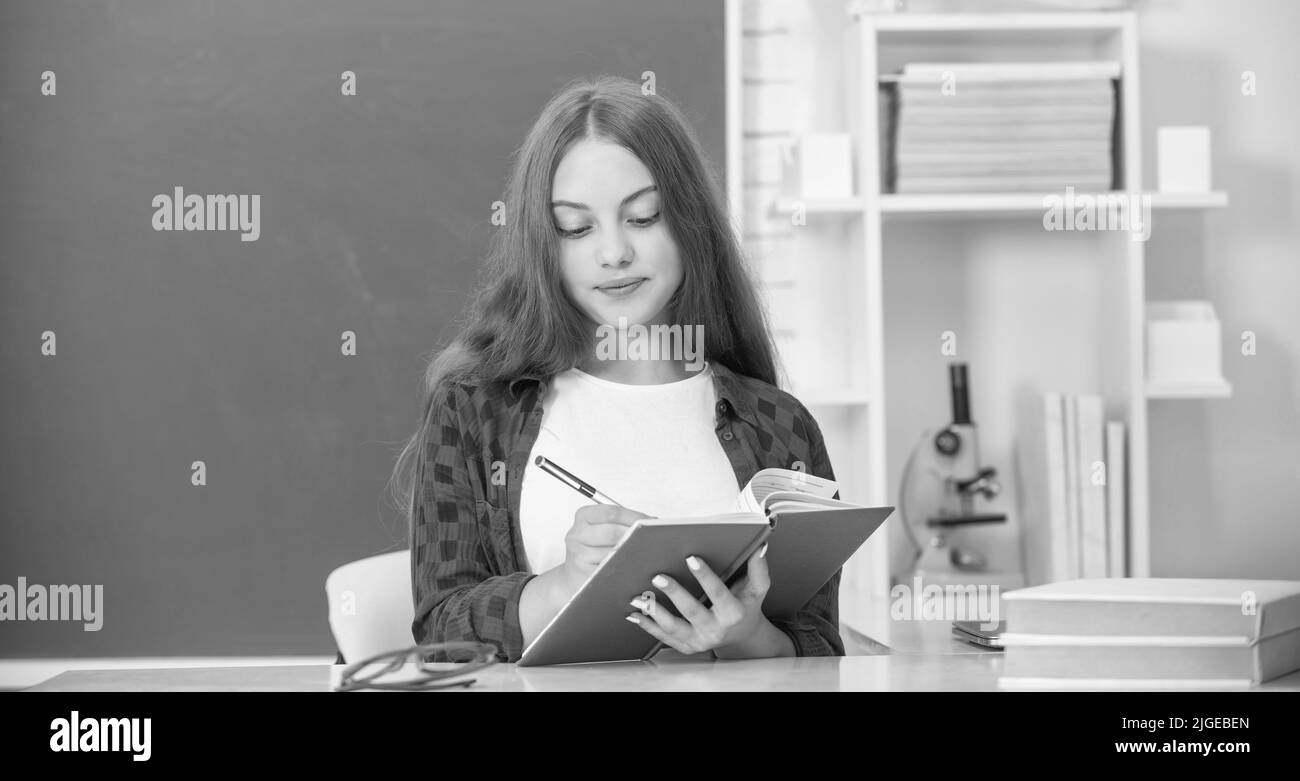 kid making notes in copybook in classroom at blackboard, erudition ...