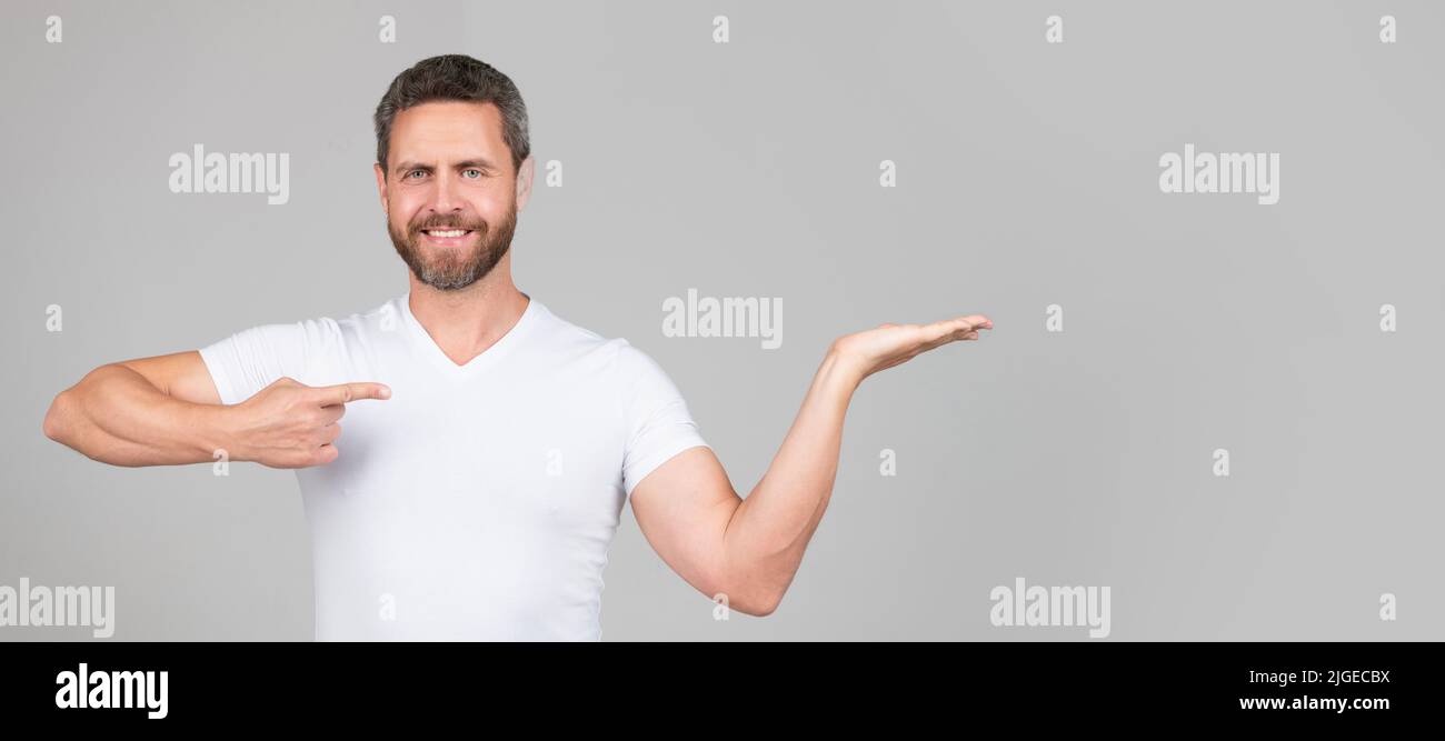 Happy handsome man smile pointing finger at open hand grey background copy space, presenting ...