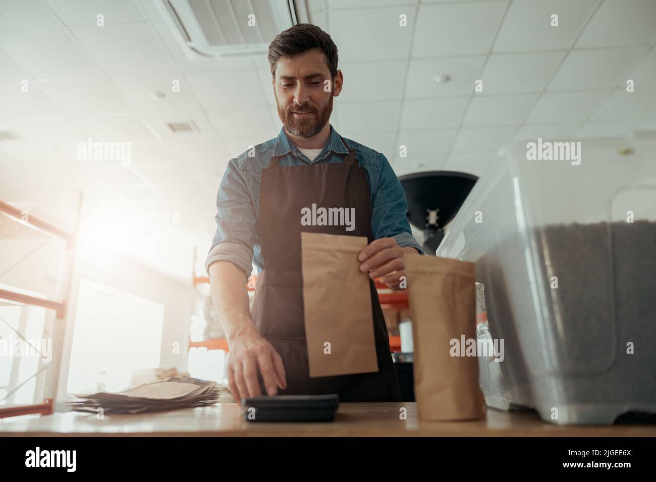 Uniformed worker packs roasted coffee beans into packages for sale ...