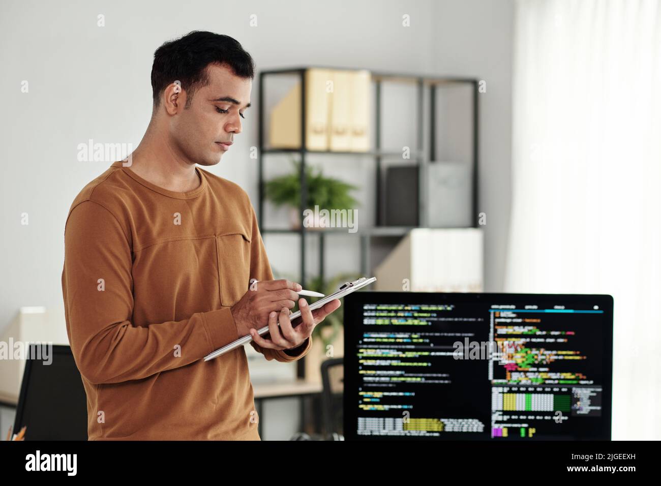Young Indian software developer writing to do list before starting work ...