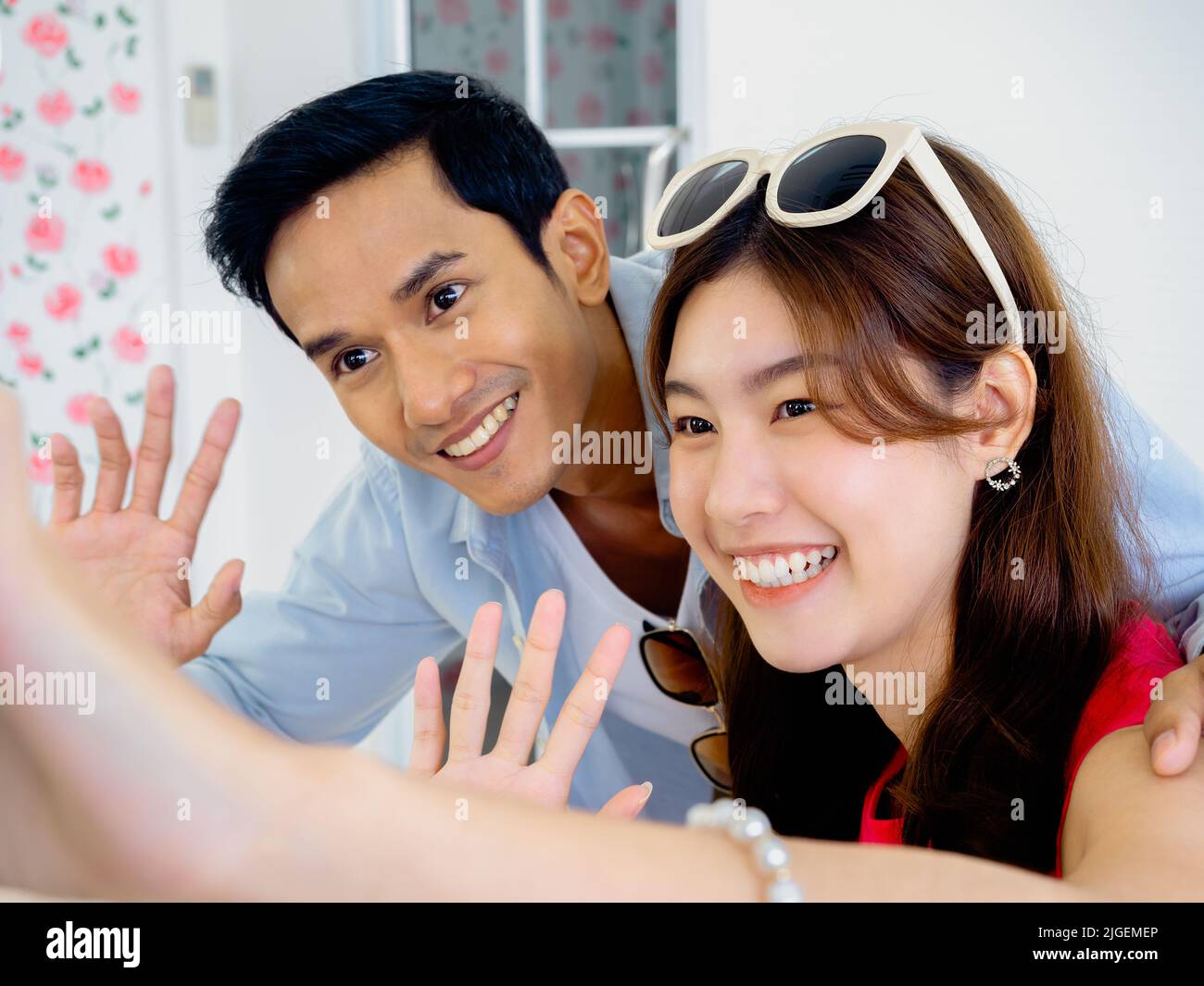 Happy young Asian couple in colorful casual shirts are waving hands in ...
