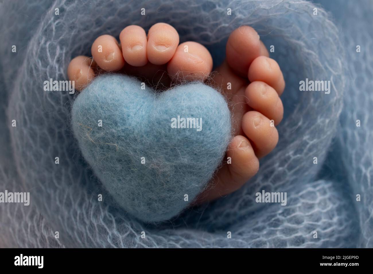 Knitted blue heart in the legs of a baby. Soft feet of a new born in a ...