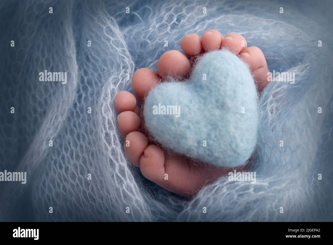 Knitted blue heart in the legs of a baby. Soft feet of a new born in a ...