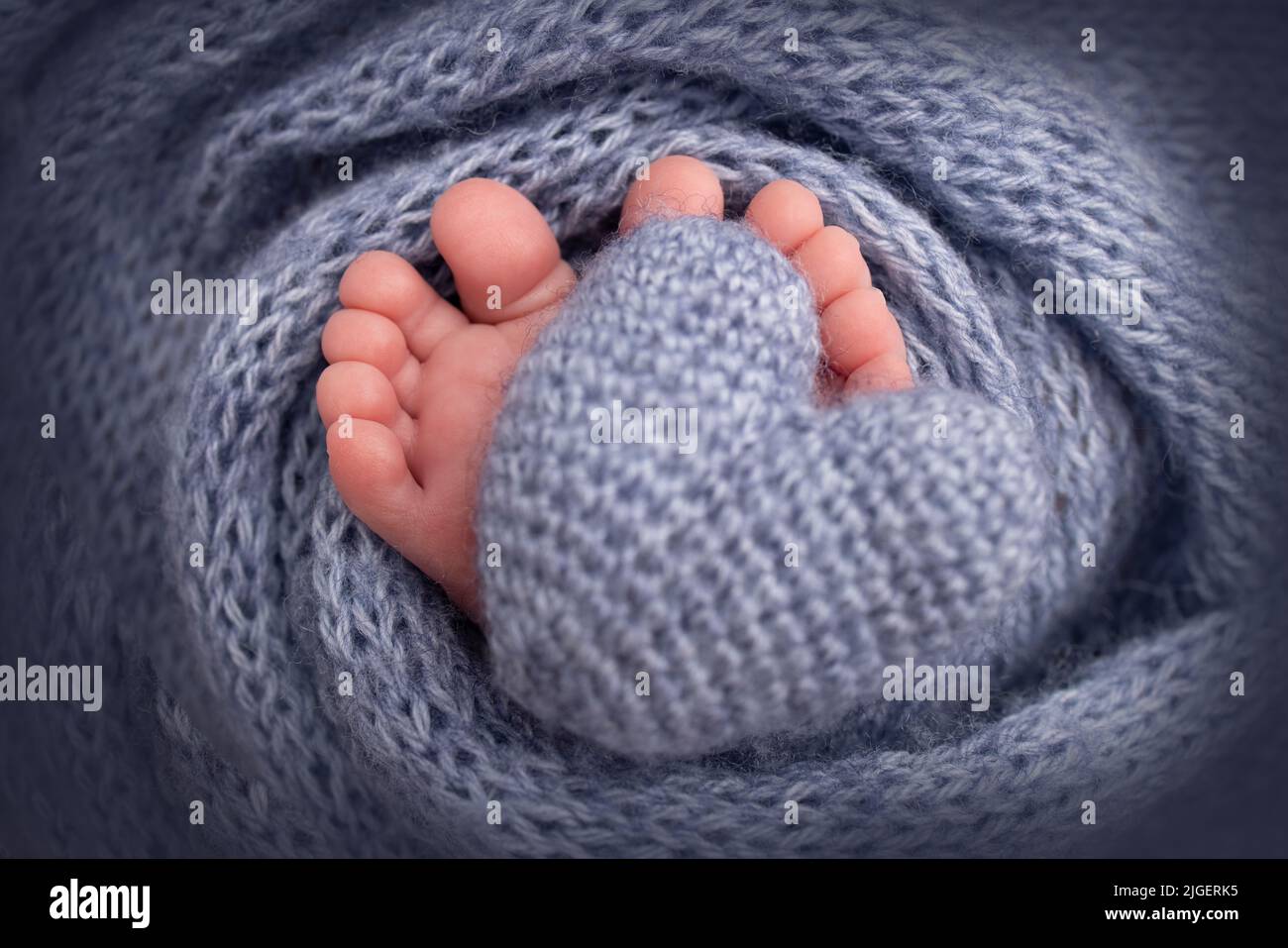 Knitted dark dark blue heart in the legs of a baby. Soft feet of a new ...