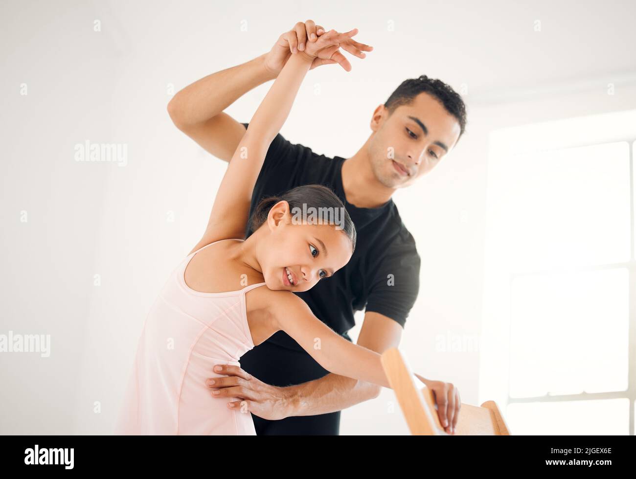 Learning a new position. a ballet teacher assisting a student with her ...