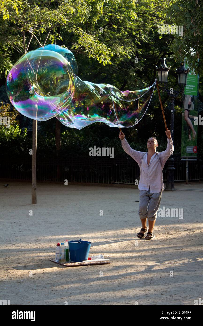 Man creating giant bubbles with a giant bubble wand in the Plaça de la ...