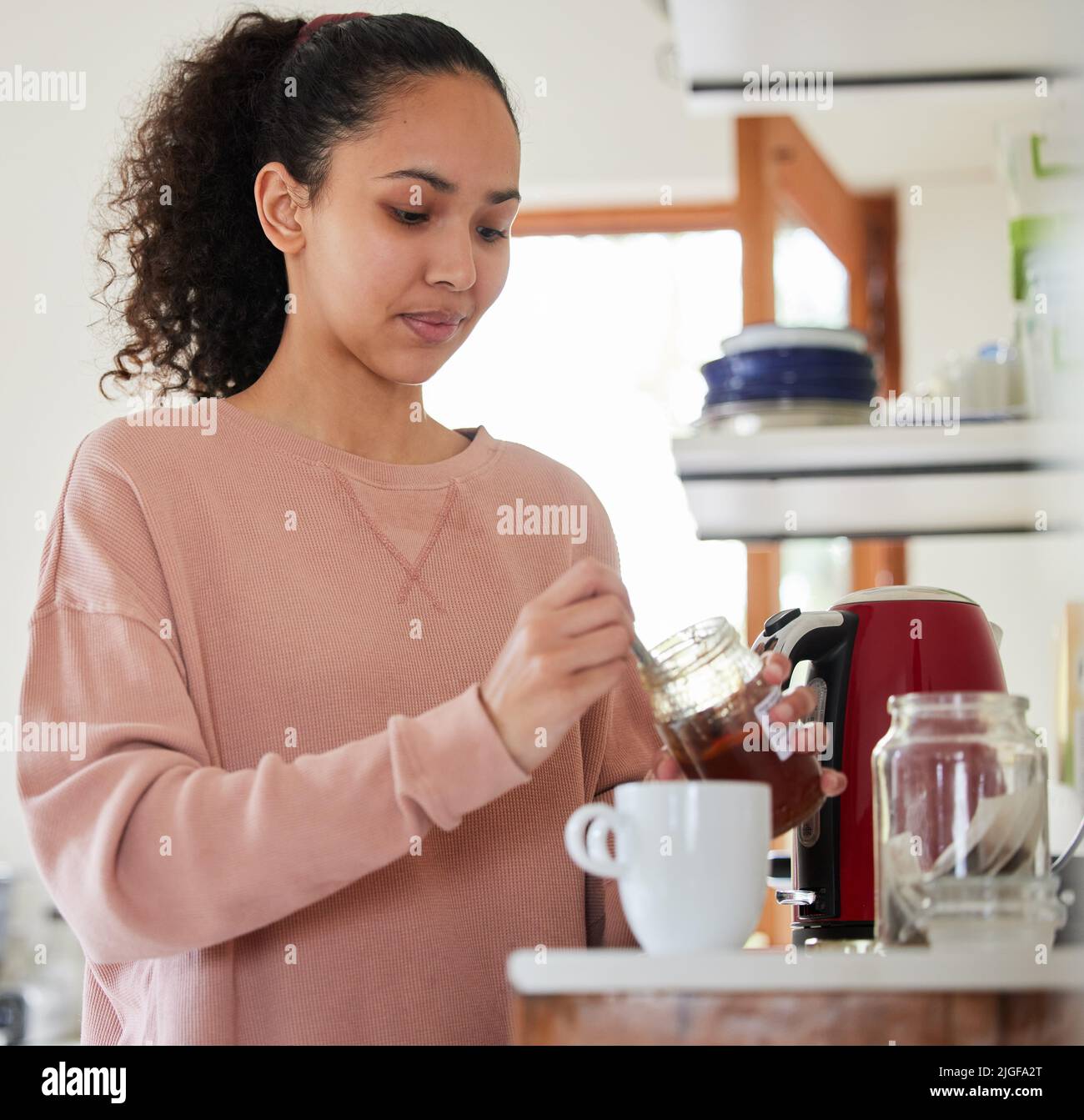 Some honey for this honey. a young woman adding honey to a cup of tea ...
