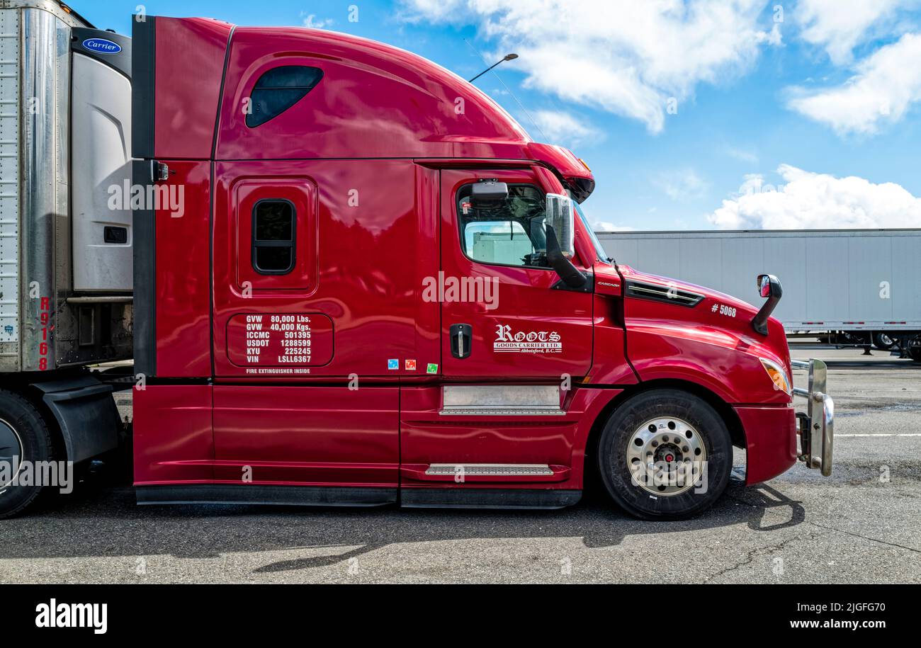 The passenger side of a red Freightliner Cascadia semi truck parked in ...