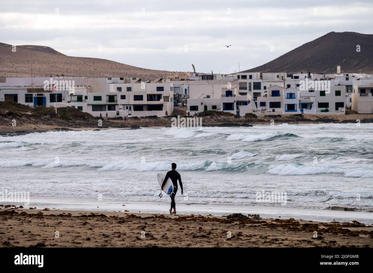 A man walks carrying a surf board in Famara Beach, in the north west ...