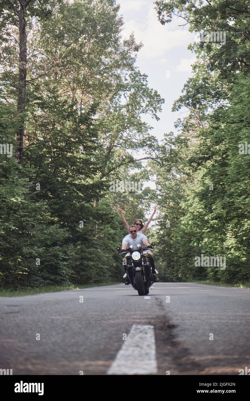 A young happy couple rides a motorcycle on an asphalt road in the ...