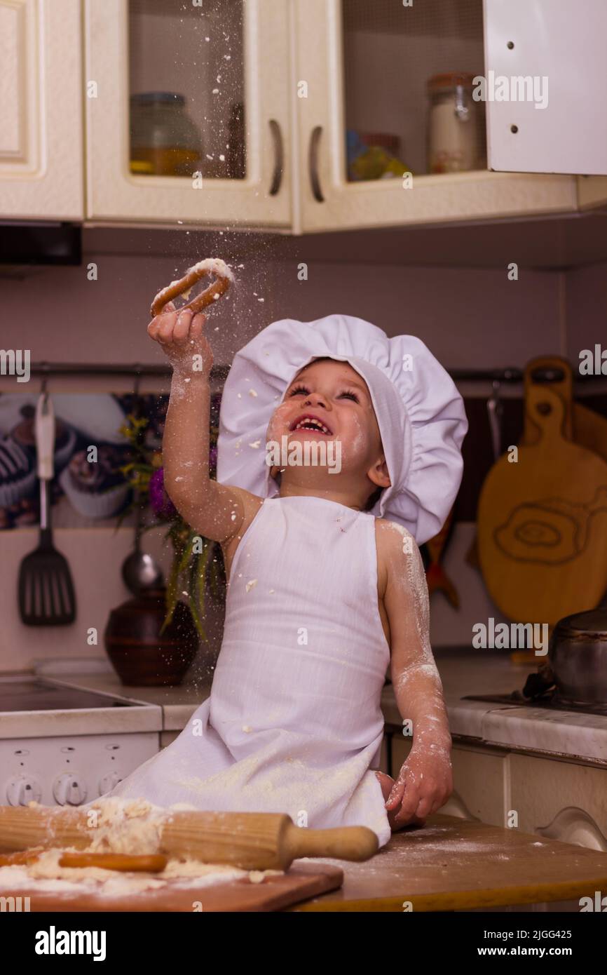 A kid in a cook's costume sits in the kitchen on a table and smiles ...