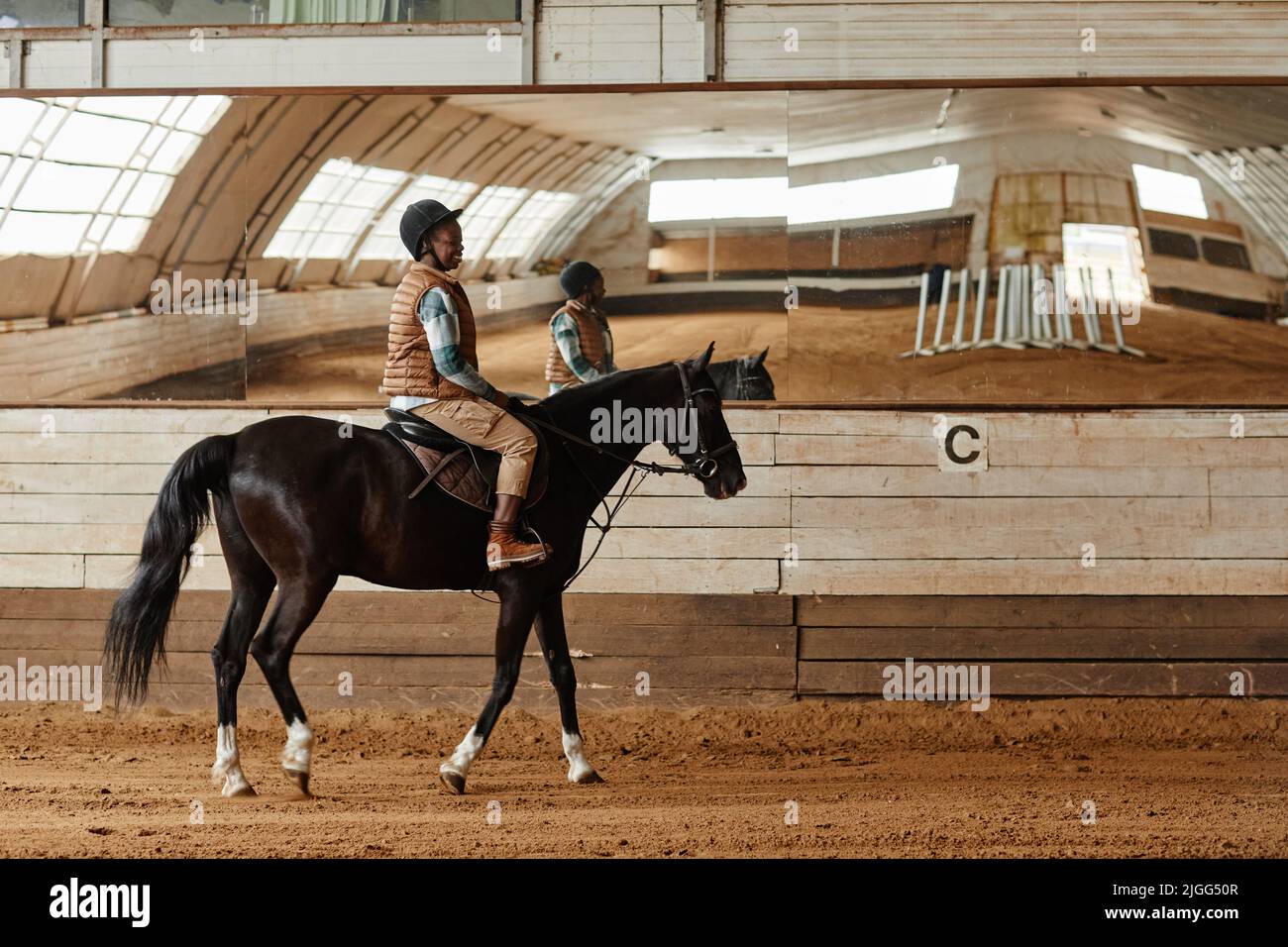 Full length side view at young woman riding horse in indoor arena or ...