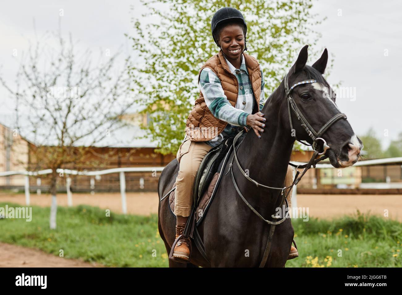 Portrait of smiling black woman riding horse in outdoor country ranch ...
