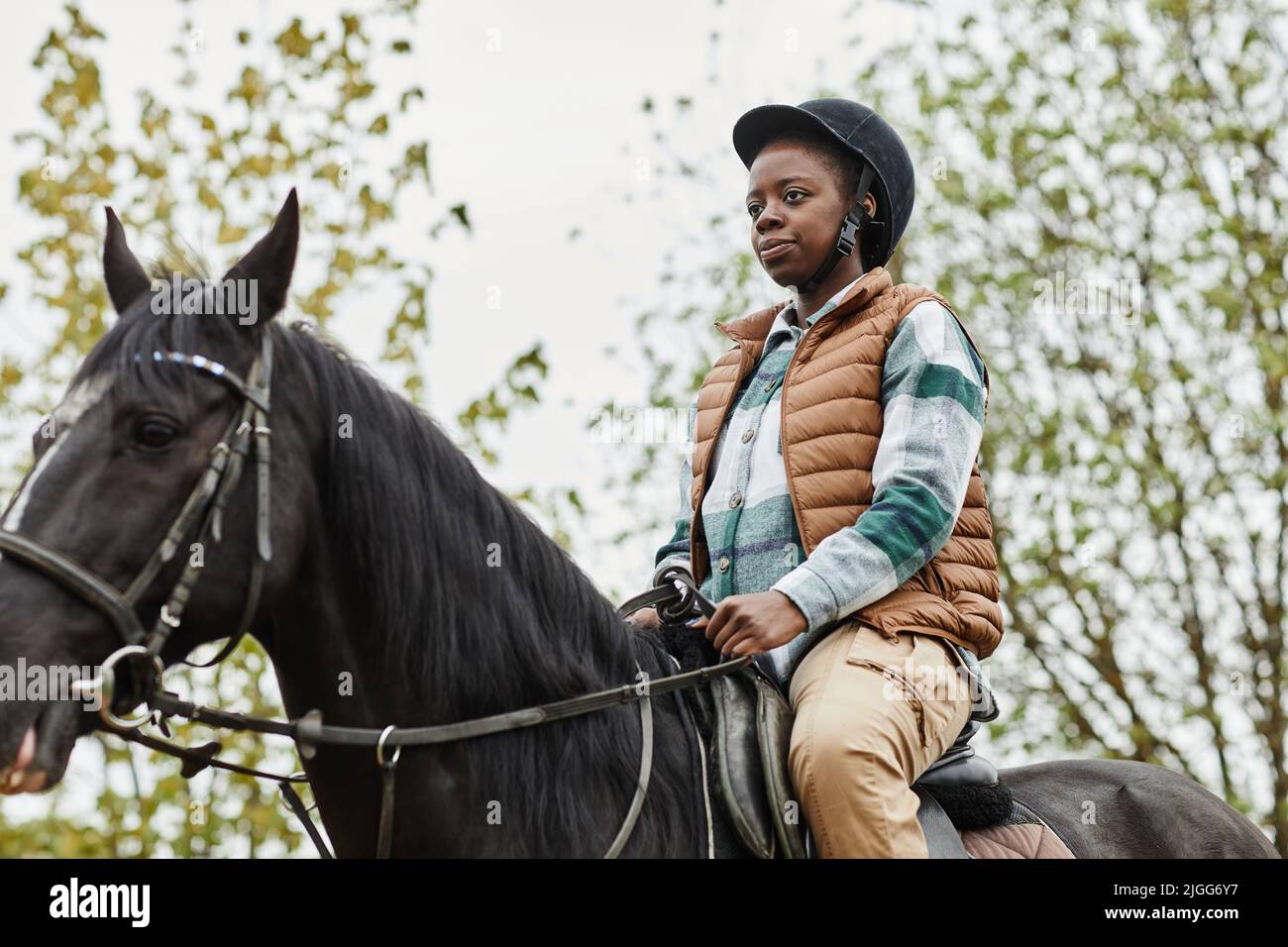 Portrait of young black woman riding horse outdoors and wearing ...