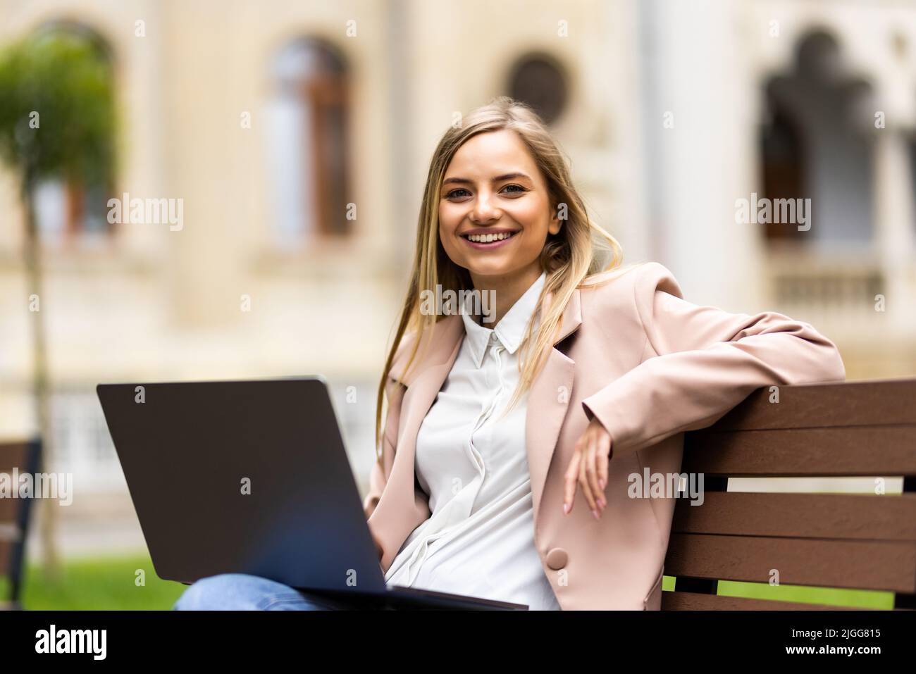 Beautiful young woman sitting in public park chatting over laptop ...