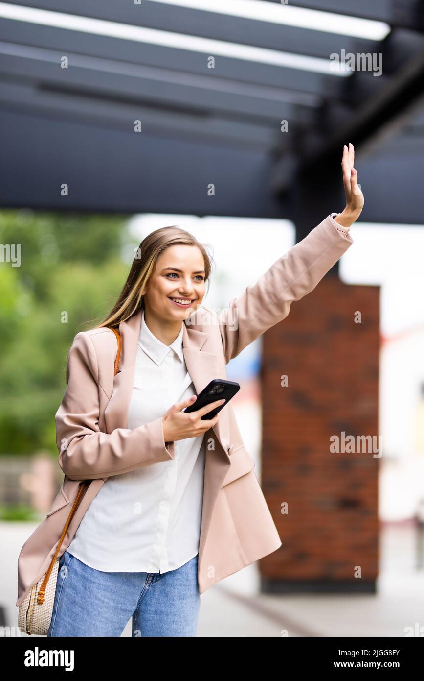 Attractive smiling lady is raising arm to say hello. She is wearing ...