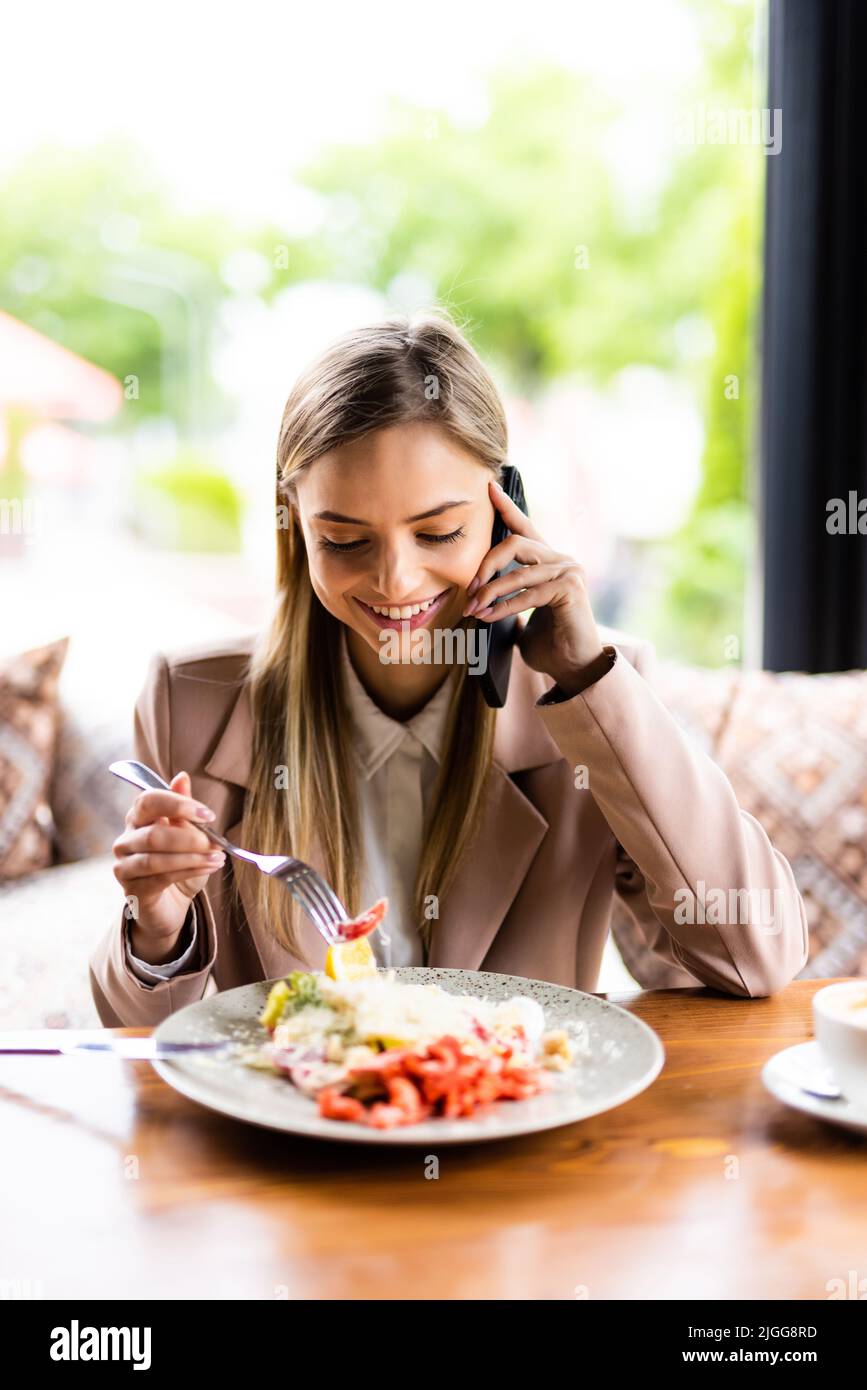 Young smiling woman sit alone at table in cafe shop eat breakfast talk ...