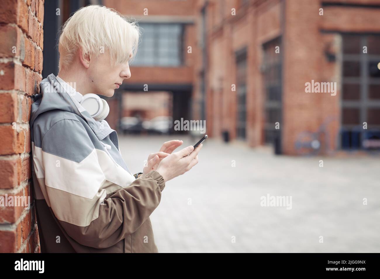 Teenage guy with blond hair standing by wall of brick building and ...